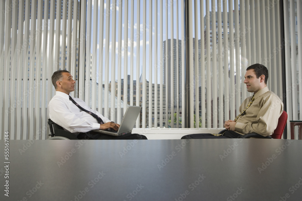 Side profile of two businessmen sitting at a conference table, one in a ...
