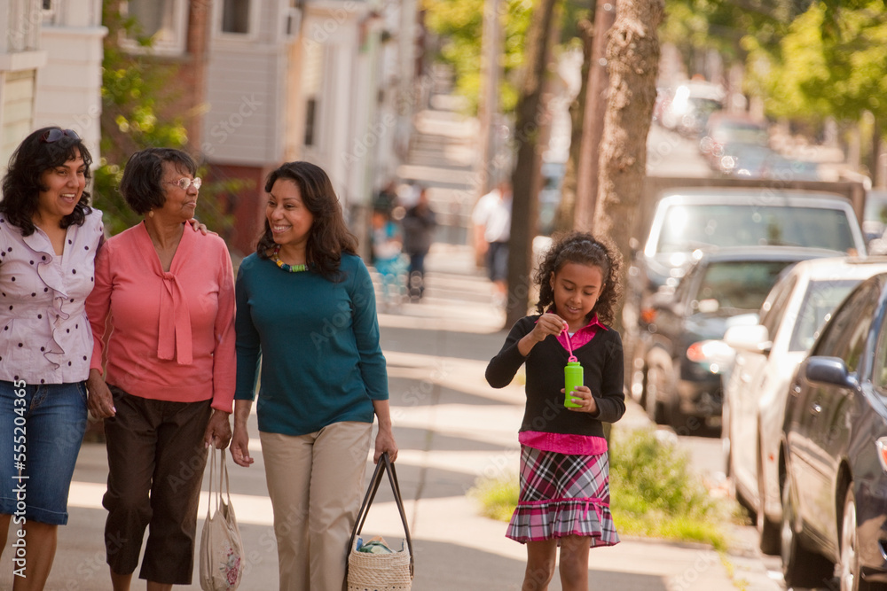 Women walking together down a sidewalk and talking and a girl blowing ...