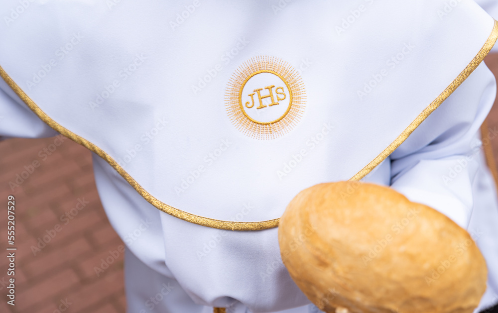 First Communion child in white alb with IHS badge holding bread with a ...