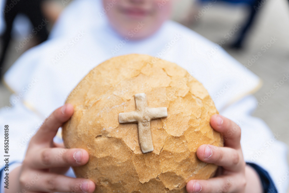 First Communion child in white alb with IHS badge holding bread with a ...