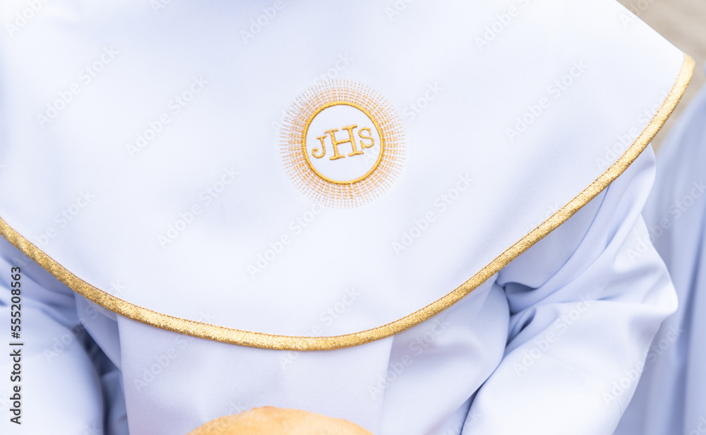 First Communion child in white alb with IHS badge holding bread with a ...