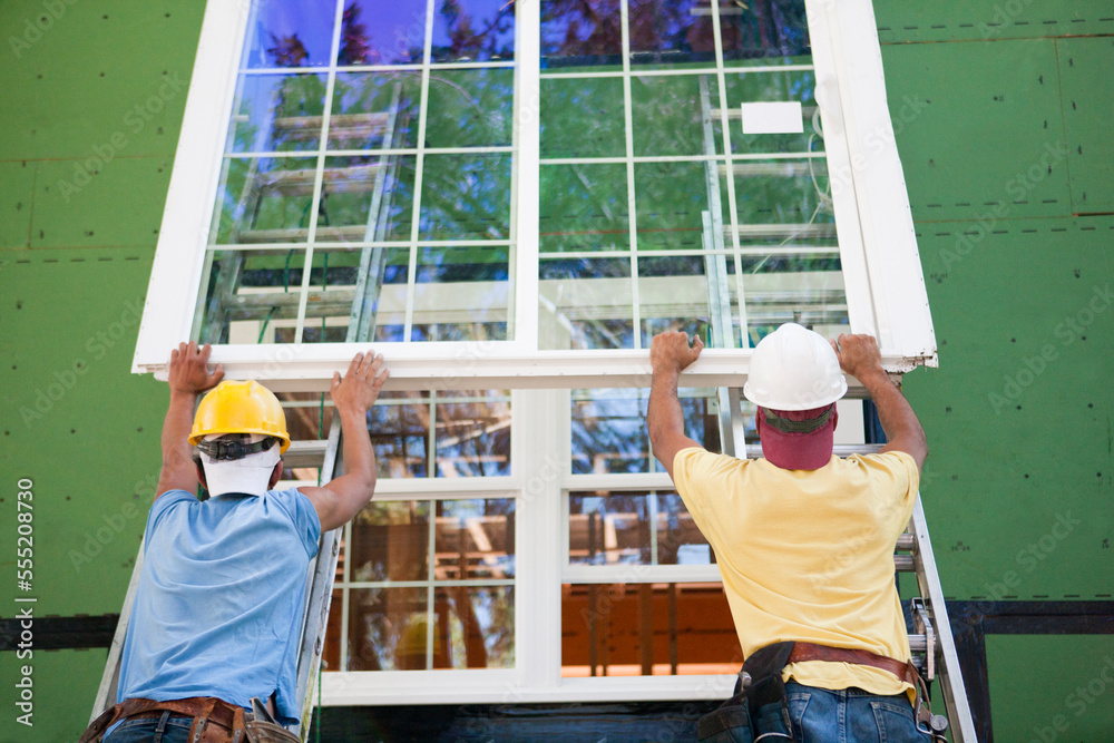 Carpenters positioning a large window frame on a house under ...