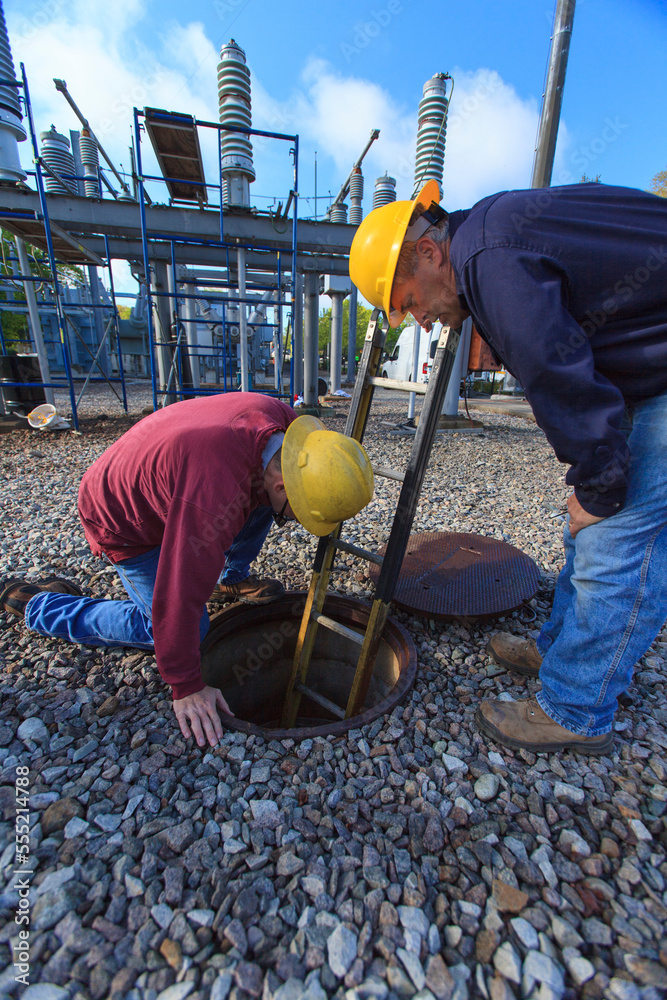Power engineers placing ladder inside manhole at high voltage power ...