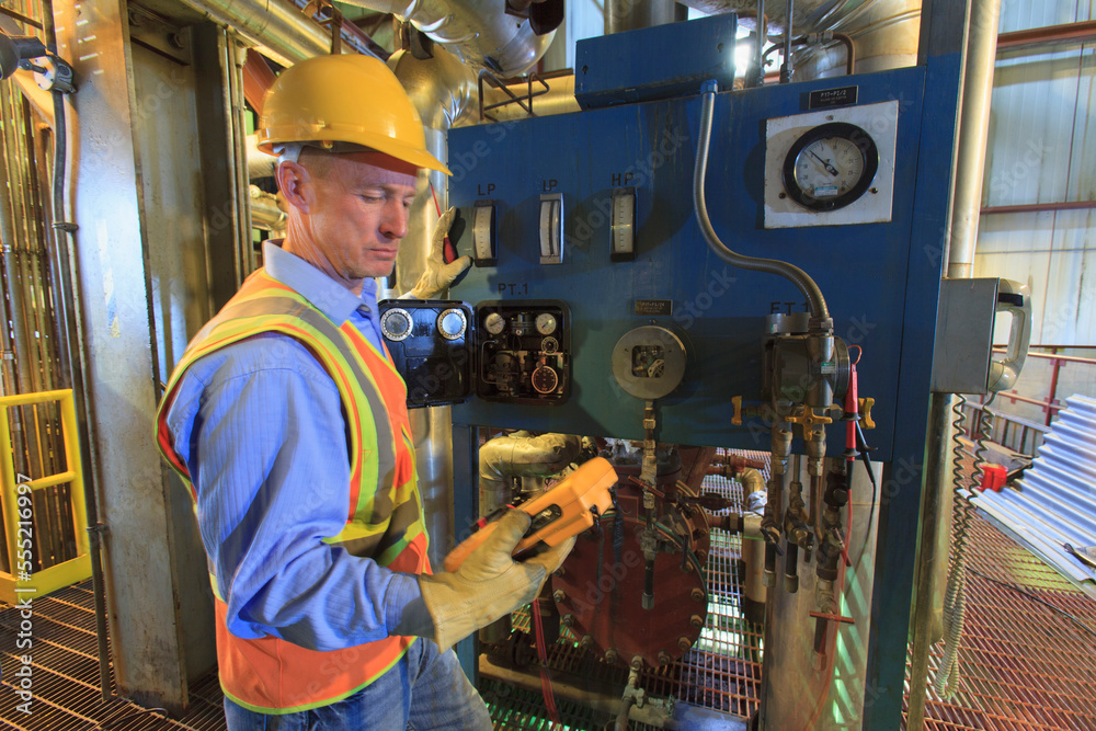 Worker wearing hard hat and reflective vest using equipment with gauges ...