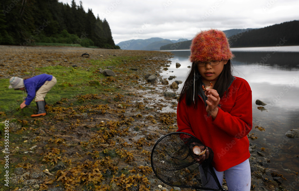 Two girls beach-comb near the water's edge investigating crabs and ...