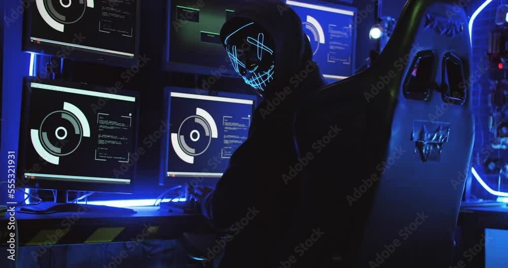A hacker wearing a mask to cover his face is using computer to hack ...