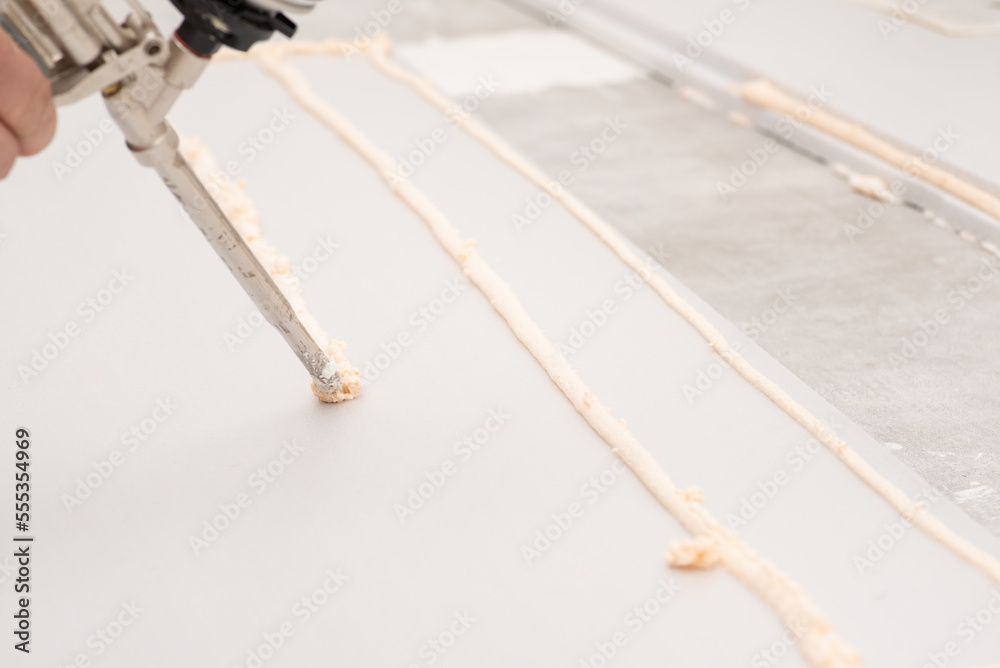 Worker applying foam with glue gun on sheet of styrofoam for gluing it ...