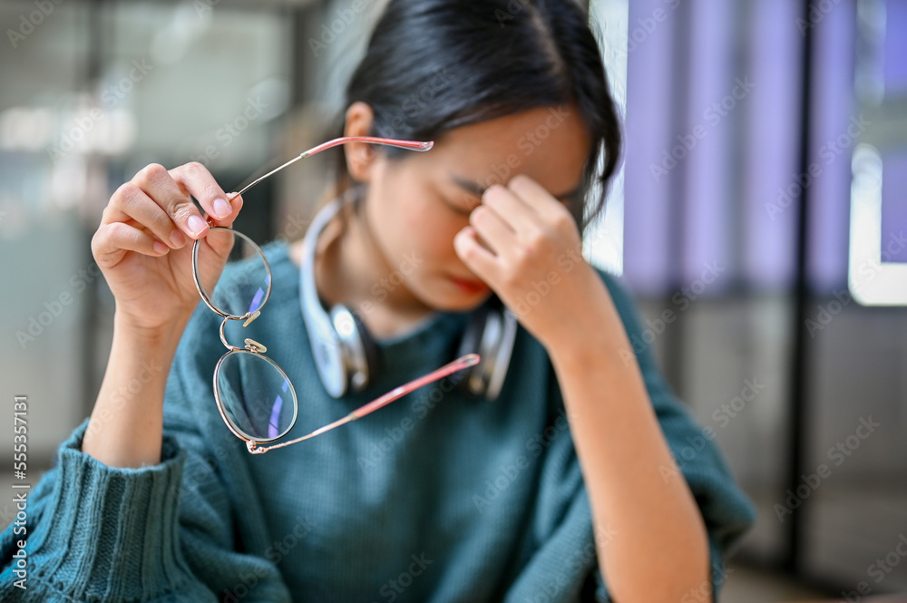 Young Asian female college student taking off her eyeglasses, suffering ...