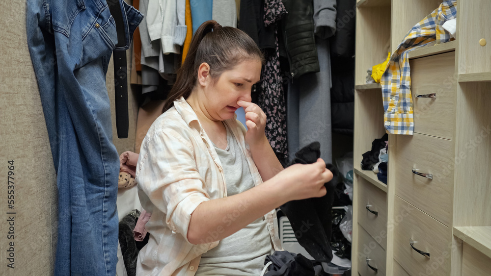 Brown-haired woman sorts dirty male clothes in walk-in closet and looks ...