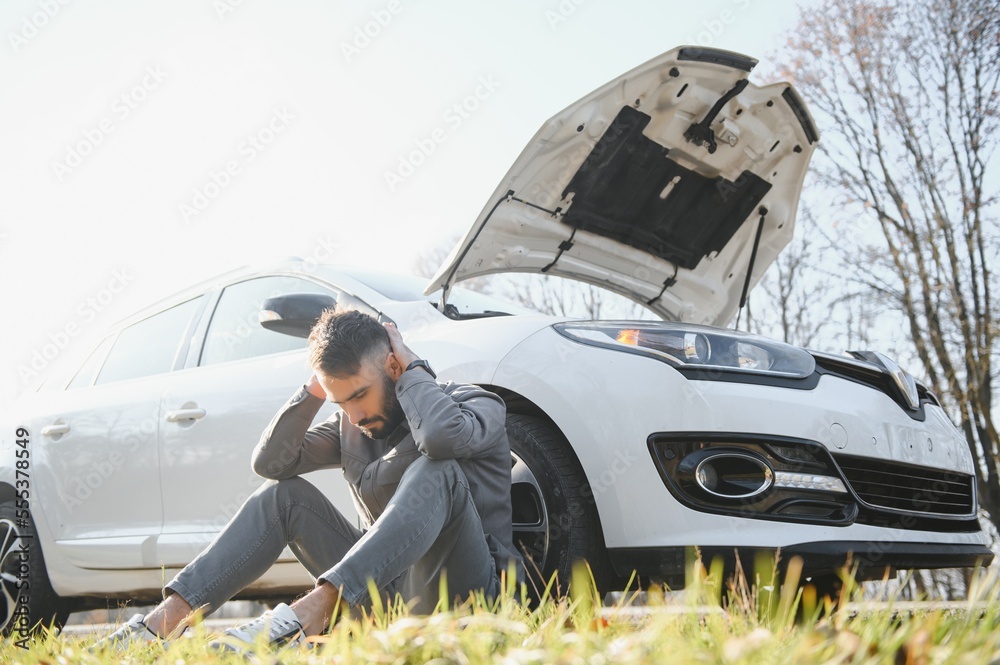 Frustrated sad upset guy driver is sitting near a broken car after road ...