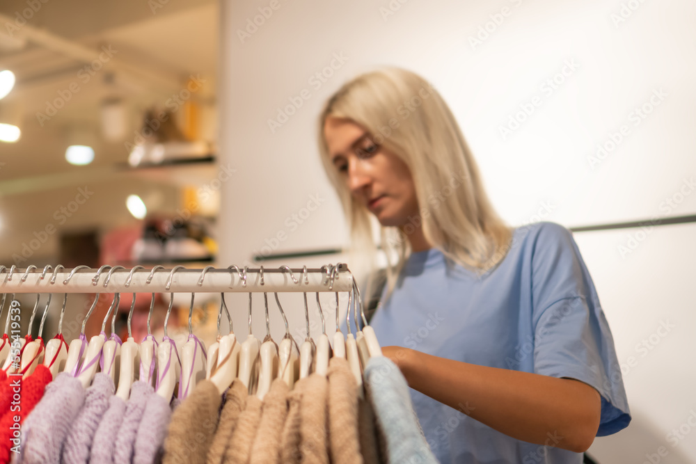 Beautiful young woman shopper is shopping at a clothing store, choosing ...