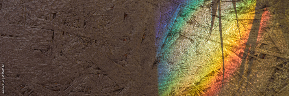 Bright rainbow light spot and shadows on textured plywood surface close ...