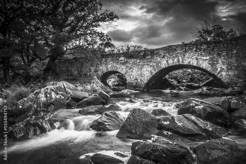 Black and white image of an arched stone bridge over a flowing river ...