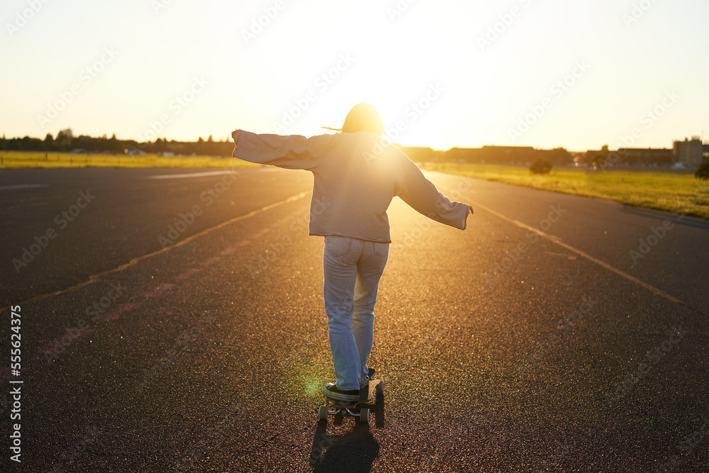 Rear view photo of young girl riding skateboard towards sunlight. Happy ...