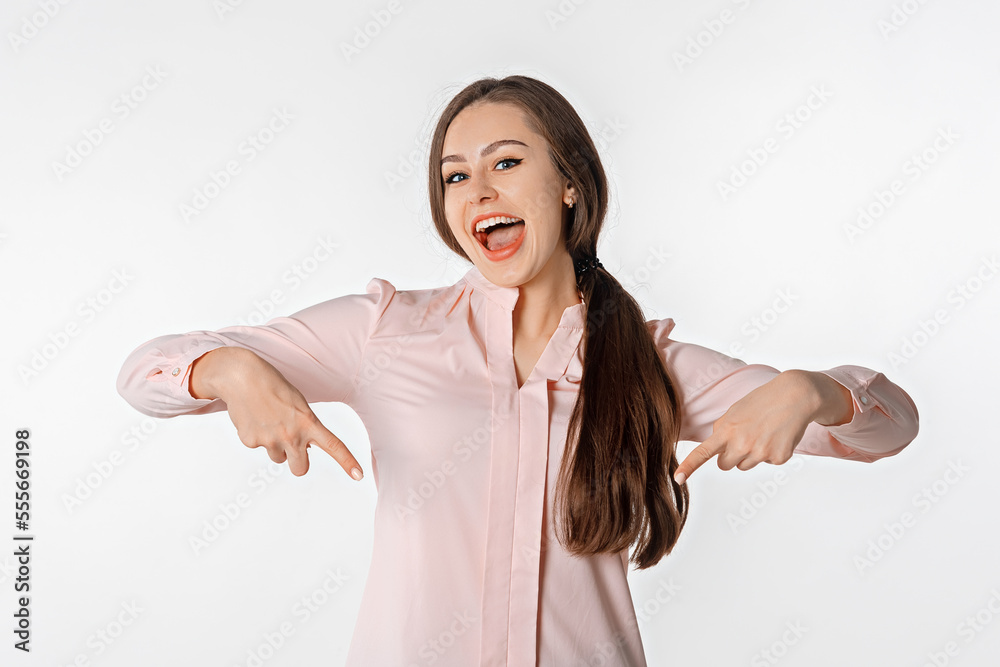 Portrait of young brunette woman pointing fingers down and smiling, showing banner, click on ...