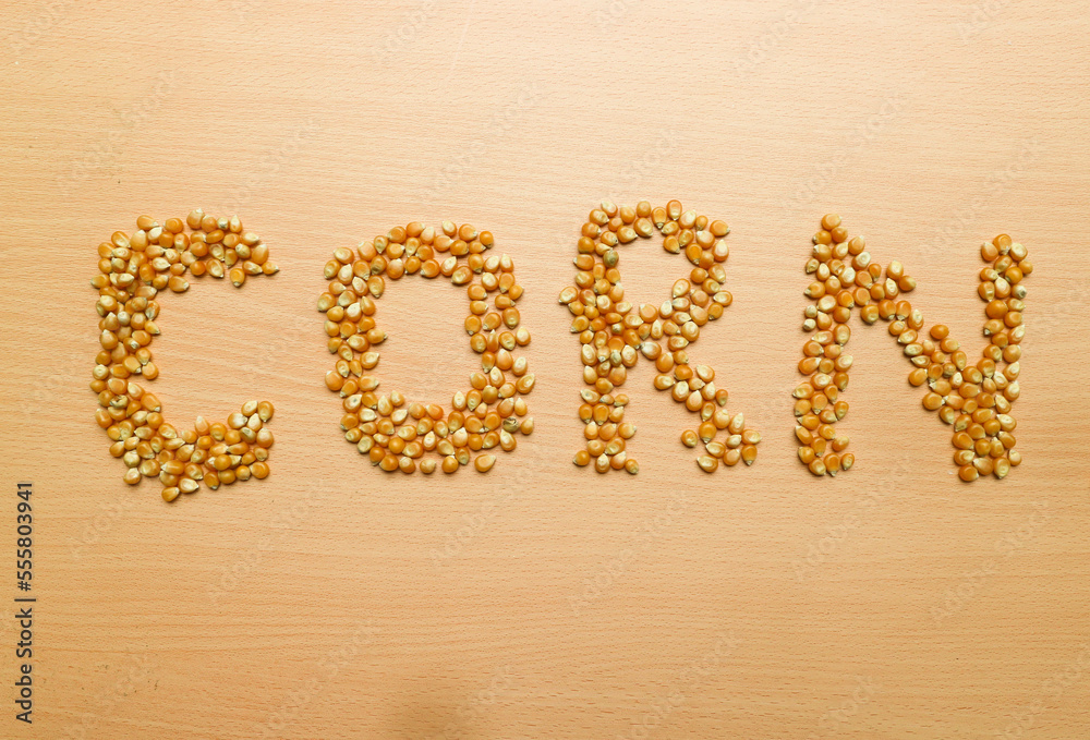 Pile of yellow corn seeds form the word 'CORN' on a brown wooden ...