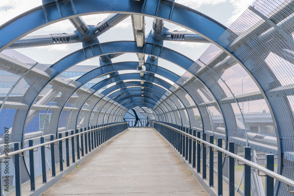 Looking down a tubular metal walkway with steel girders and railings ...