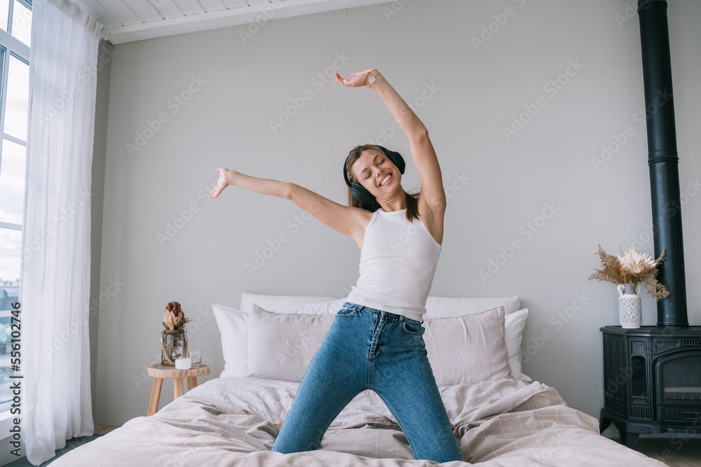 Excited caucasian girl dancing on bed in headphones eyes closed with ...
