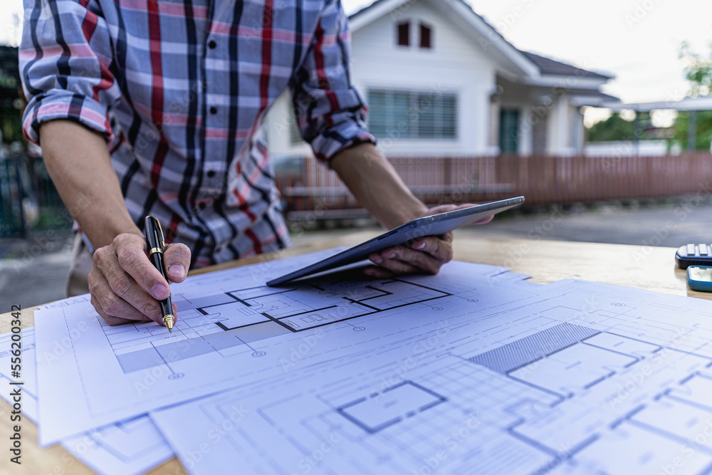 Engineer pointing at blueprint and using laptop to draw building design ...