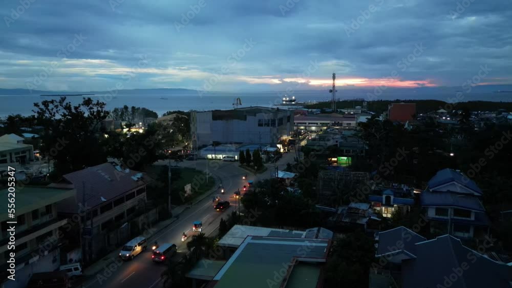A small Philippine town in the coming dusk of the night. Cars drive ...