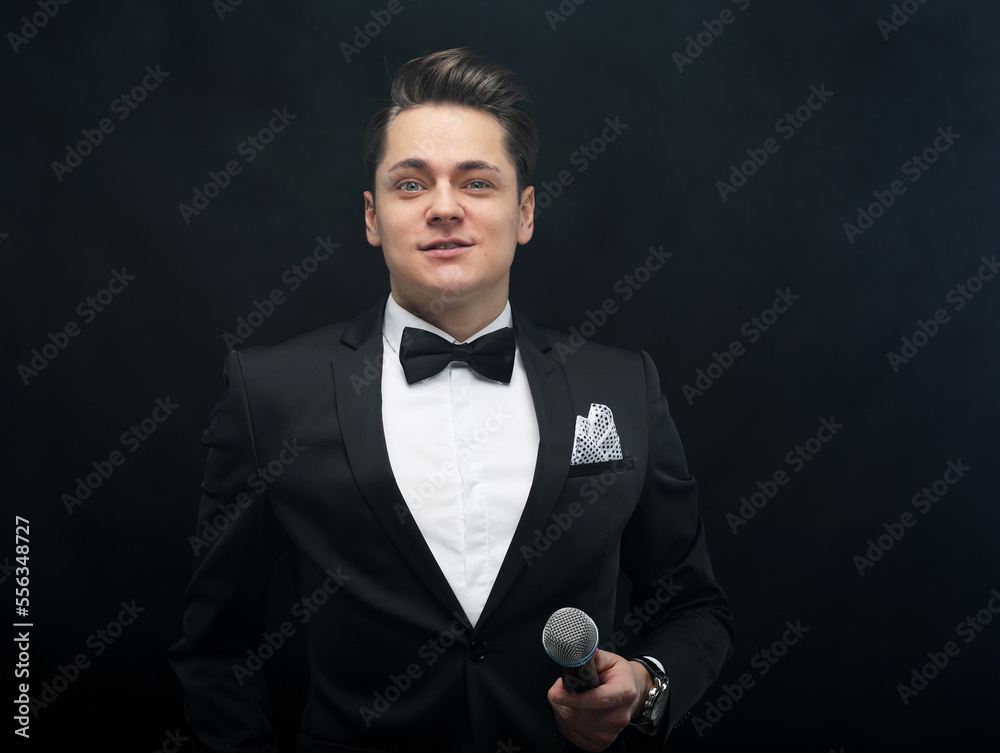 Stylish young man in a tuxedo holding a microphone, posing against a ...