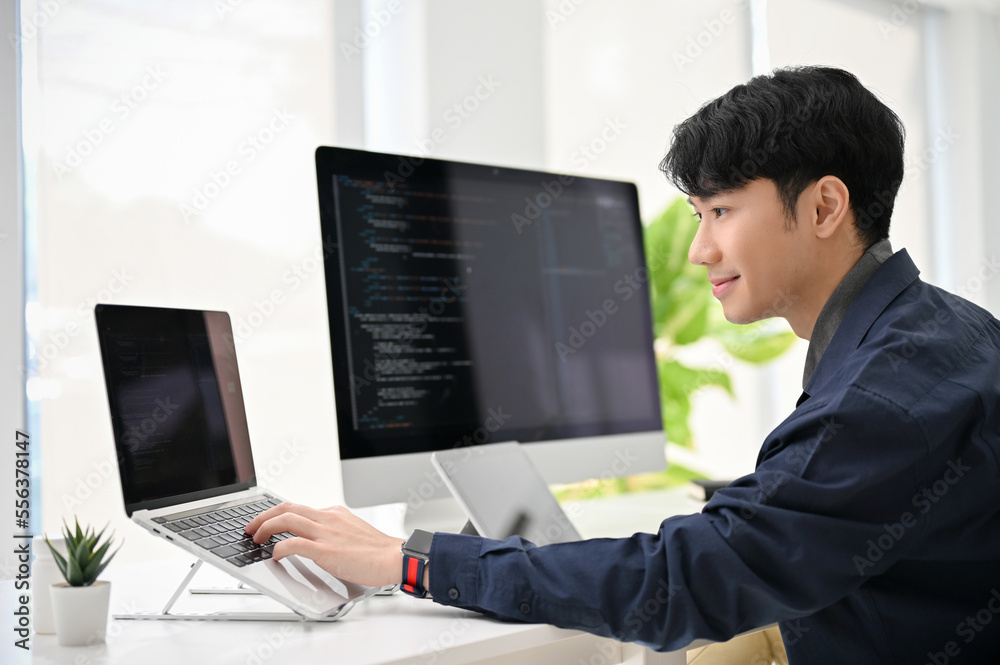 Smart young Asian male programmer coding at his desk, using laptop and ...