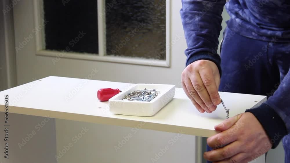 A man fastens the cover of the rack with euro screws. Wooden modular ...