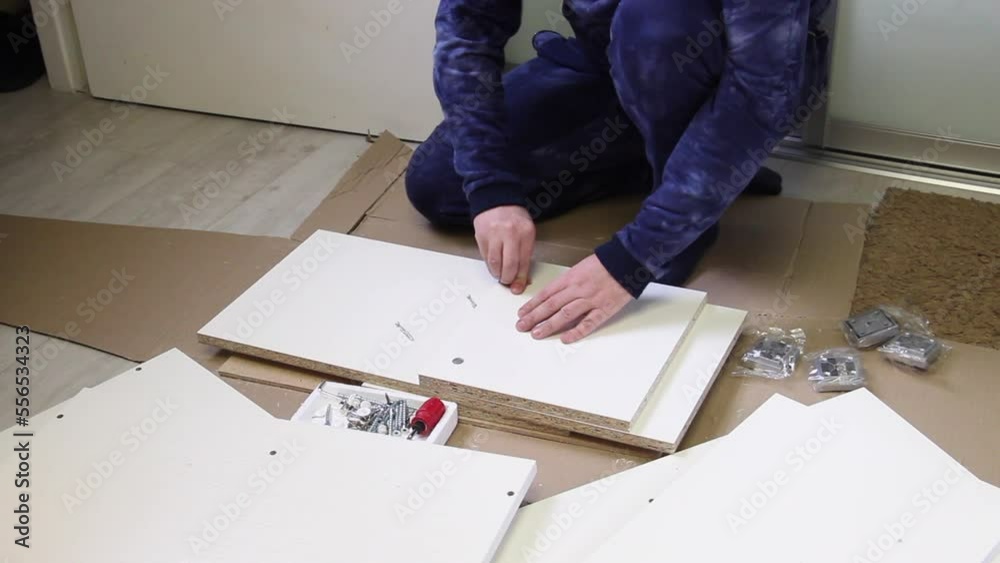 A man installs an eccentric in a wooden panel. Screws in the eccentric ...
