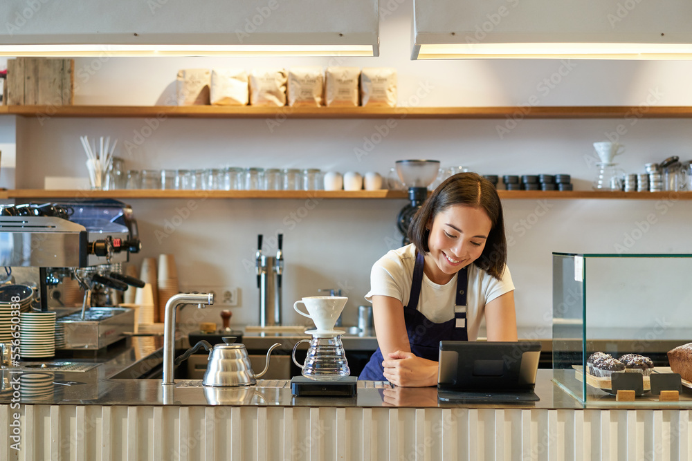 Happy smiling asian barista, girl behind counter, working with POS ...