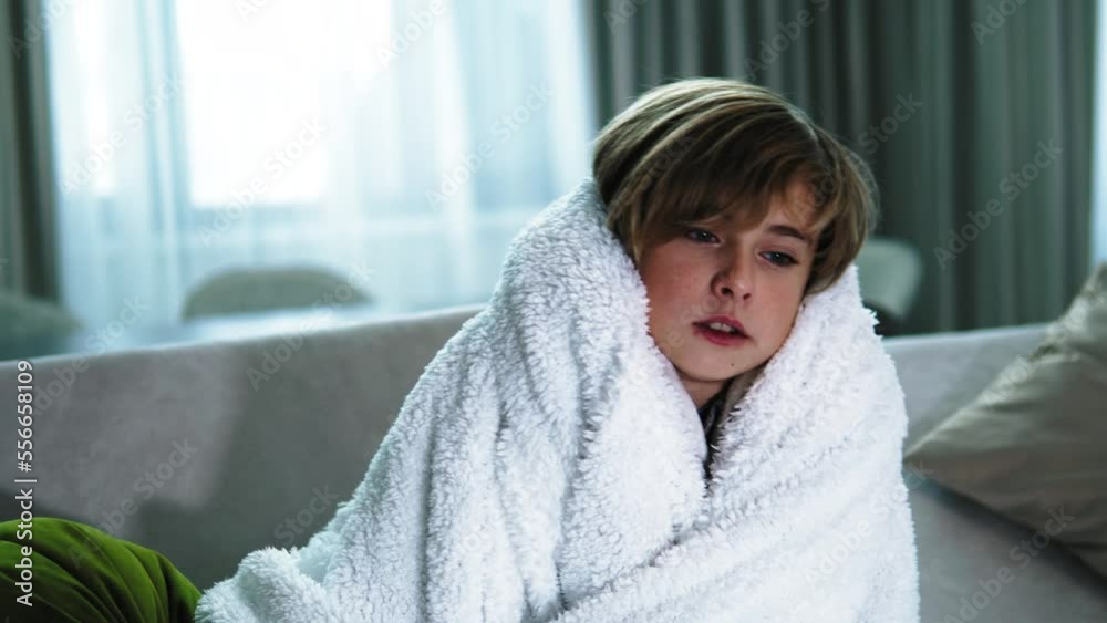 Little boy is cold, sitting on the sofa with a blanket. No heating at ...
