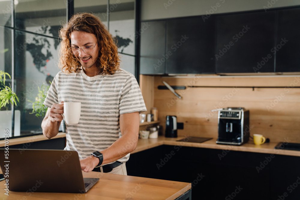 Foto de Young man drinking coffee while working on laptop in office ...