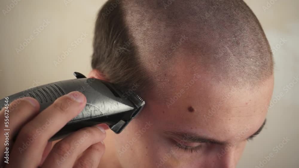A handsome man cuts his own hair with a trimmer, a machine at home ...