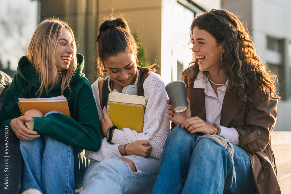 Front view of three college students sitting in front of the university ...