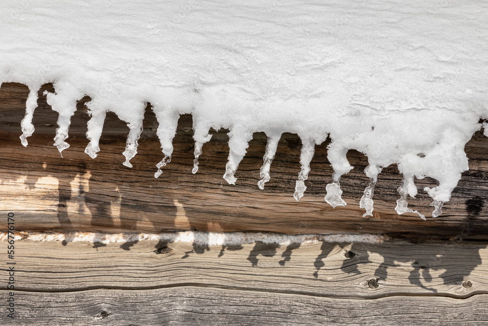 Detail photograph of melting snow hanging from the eave of a log cabin ...