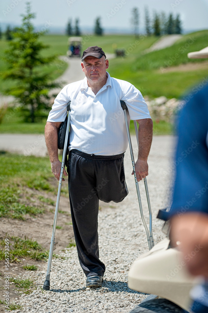 Man with amputated leg stands with crutches on a gravel path on a golf ...