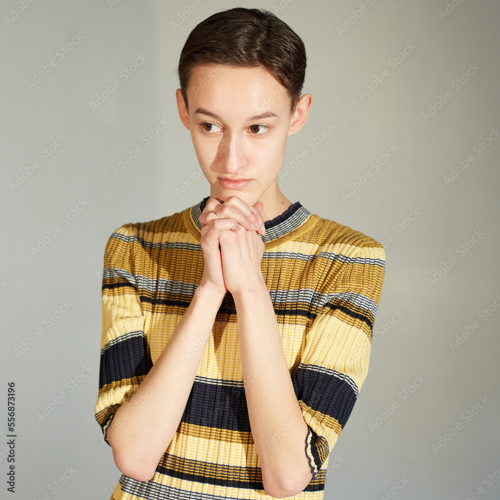 Pretty gender neutral model in striped dress clasping hands and looking ...