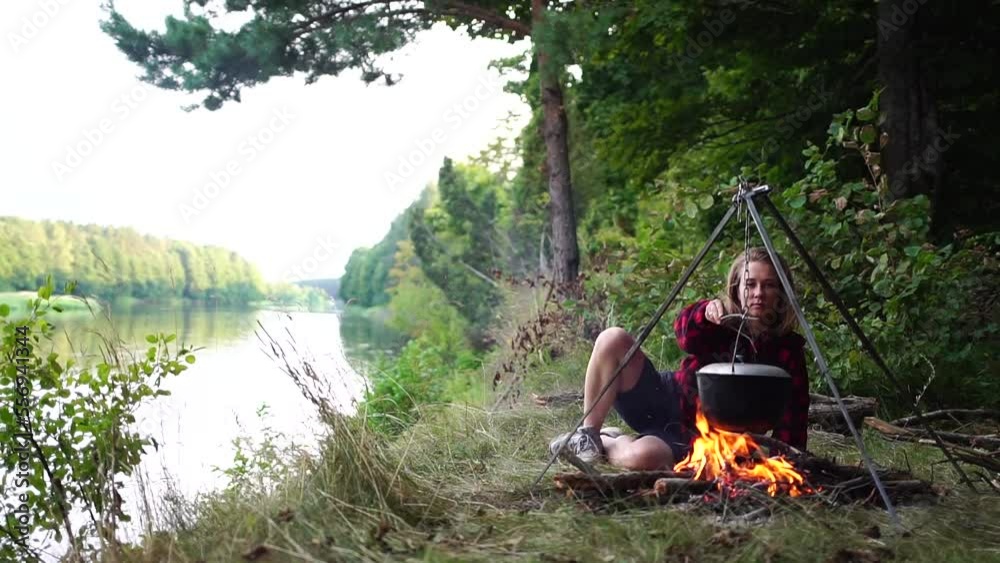Cooking over a campfire at a campsite. A girl cooks food in nature at ...