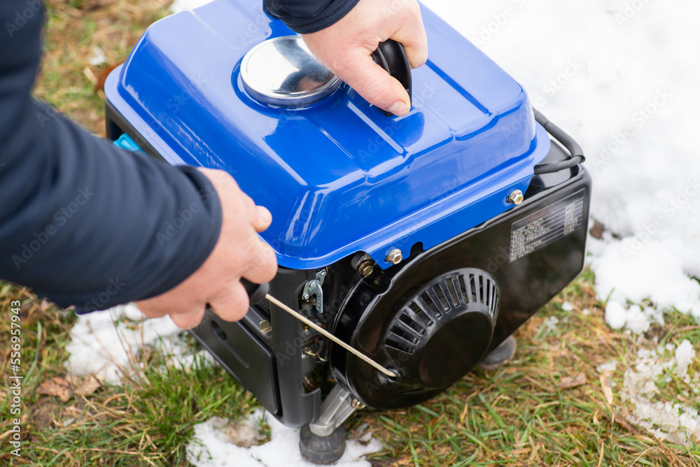 Man's hand starts a gasoline electric generator standing on the grass ...
