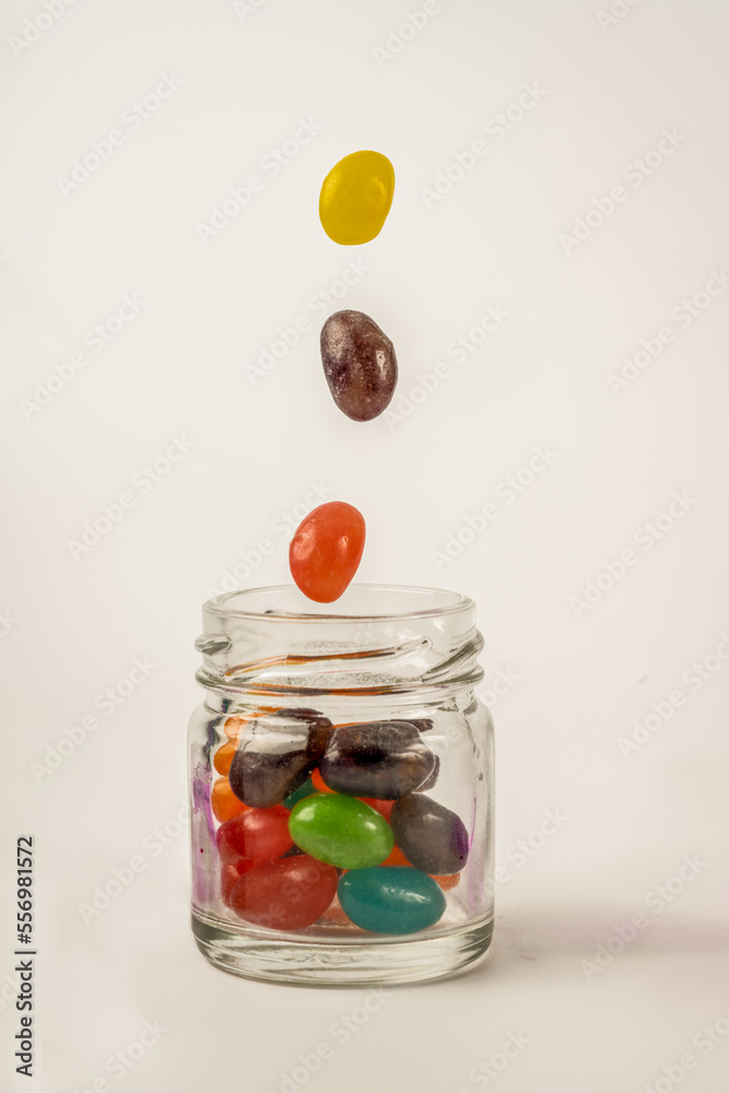 falling colorful jelly beans dropping into a glass screw top jar ...