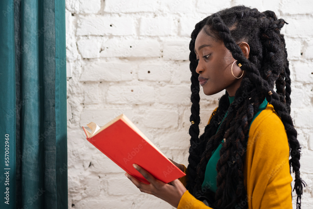 Portrait of a young African girl reading a book in a vintage library ...