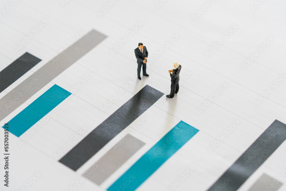 Miniature businessman leader standing with bar graph and chart of ...