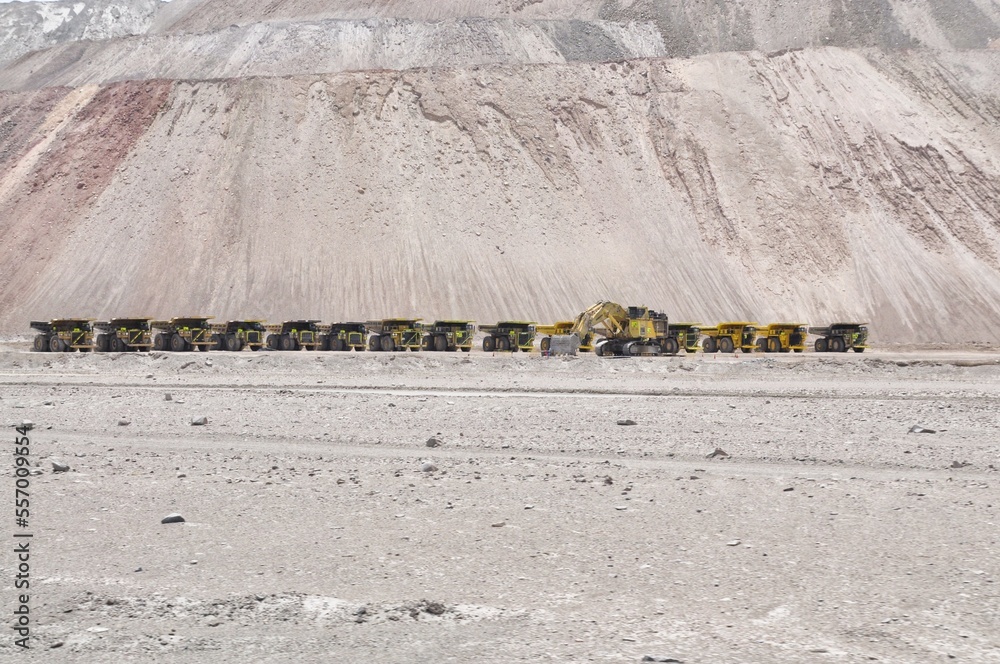 Huge mining trucks are parked in a row in front of a big hill. Mining ...
