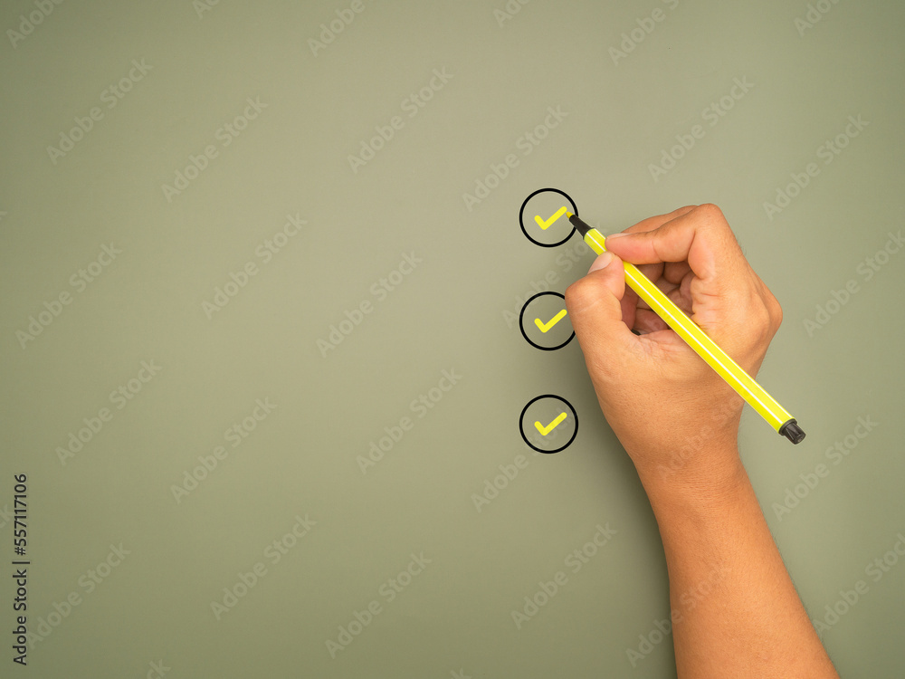 Hand holding a pen check-marking on the checklist box on a green ...