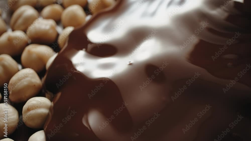 Close-up whole hazelnuts pouring with hot melted chocolate, flowing ...
