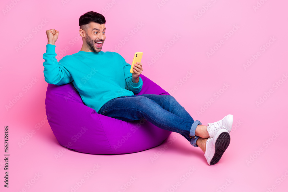 Full body photo of young nice guy sit bean bag hold device winner raise ...