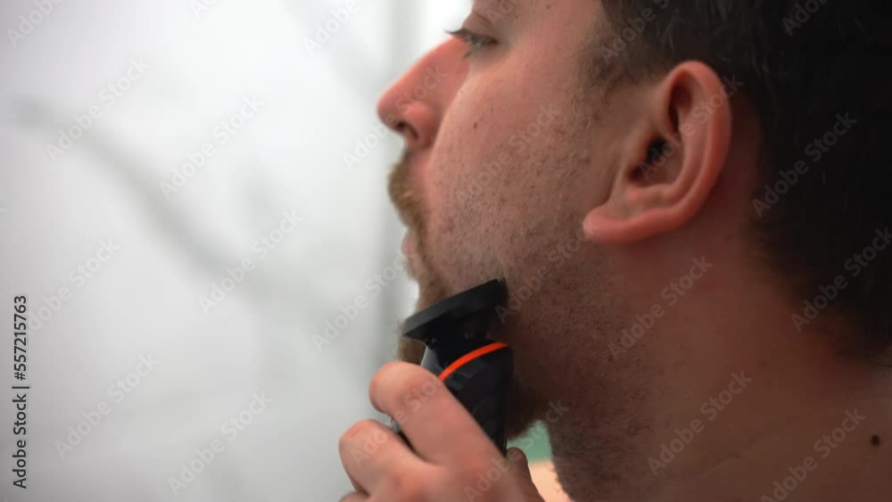 Shaving beard with electric trimmer, man in profile removing facial ...