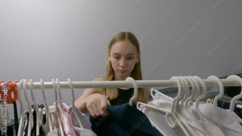 Blondy cute teen girl is choosing clothes hanging on the racks in her ...
