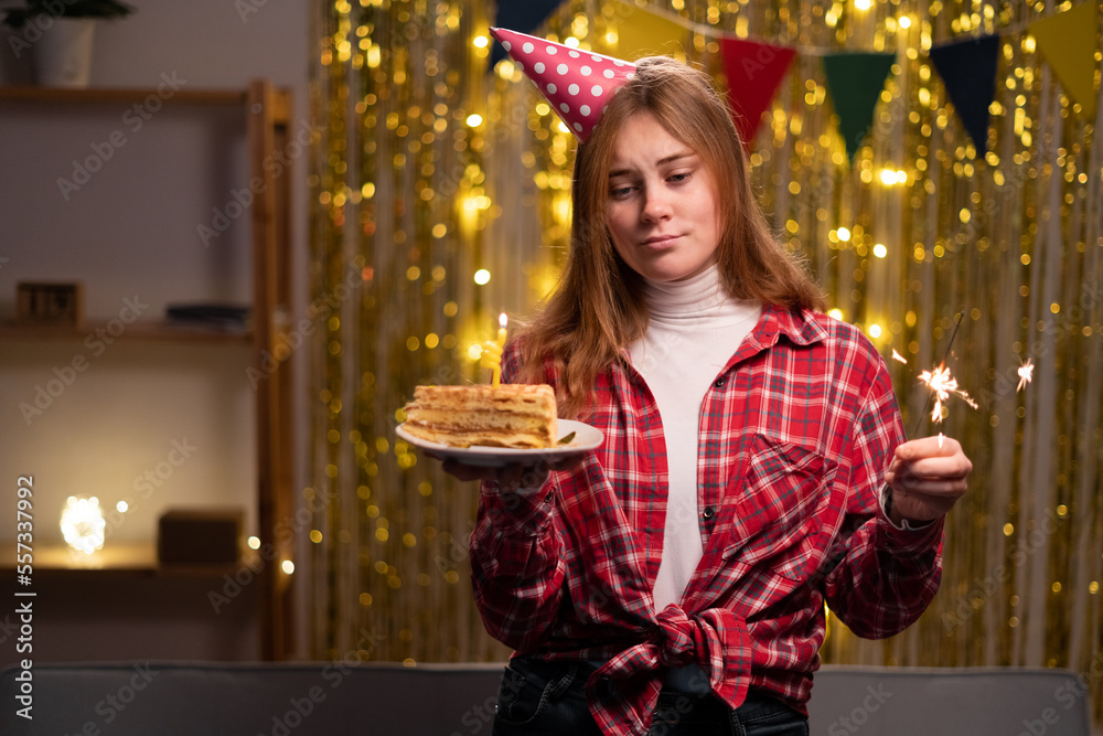 Upset displeased girl at her birthday party holding a cake and ...