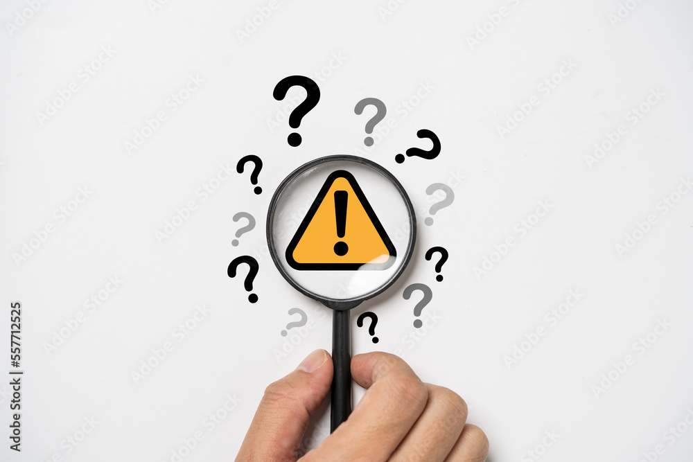 Hand holding magnifier glass with yellow triangle caution warning sign ...