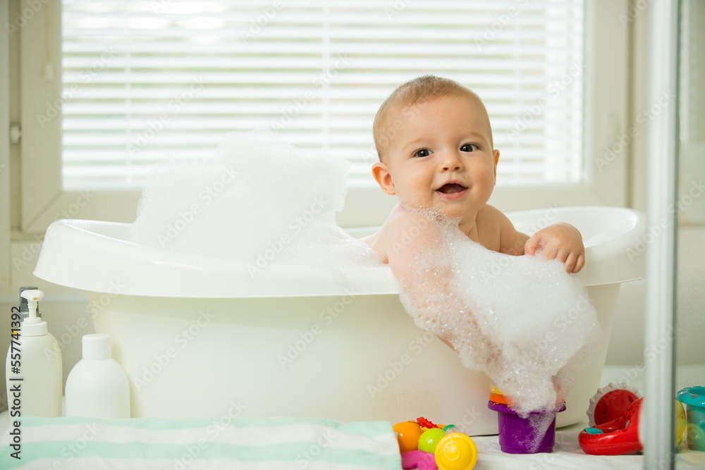 Cute little baby sitting in white bathtub with foam and soap bubbles ...
